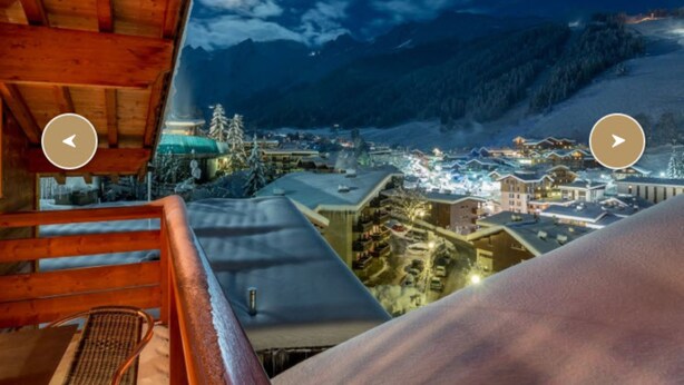 Vista de uma varanda com vista para uma cidade montanhosa nevada à noite.