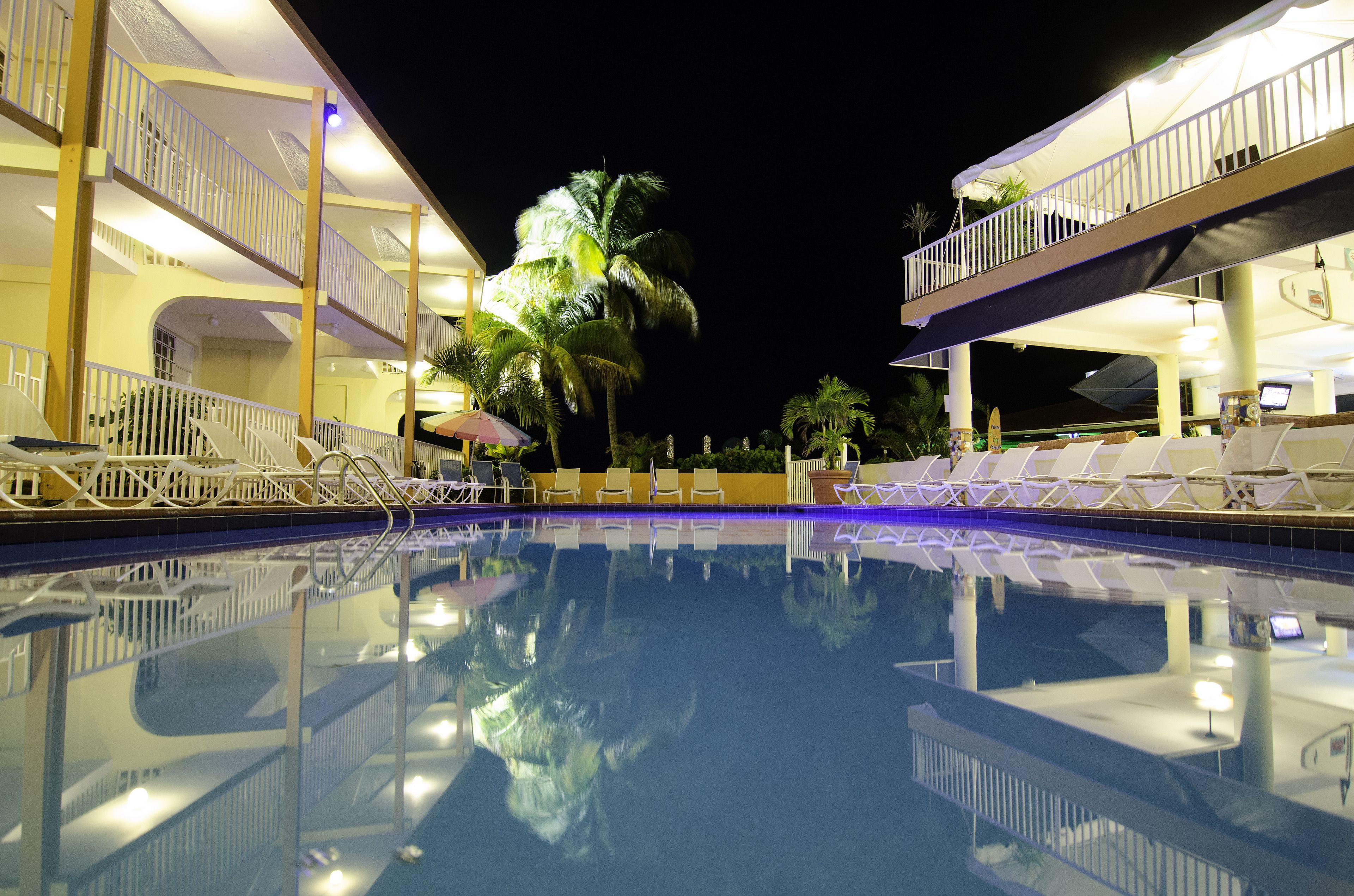 Vista noturna de uma área de piscina de hotel com água cristalina refletindo o ambiente.