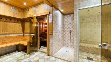 Área de sauna com bancos de madeira e porta de vidro para uma área de chuveiro com paredes revestidas de azulejos.