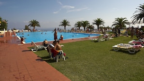 Uma área de piscina com várias piscinas, espreguiçadeiras e palmeiras.