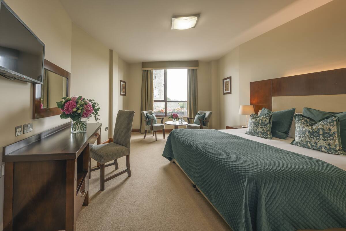 Quarto de hotel com cama, escrivaninha, cadeira, televisão e janela com cortinas.