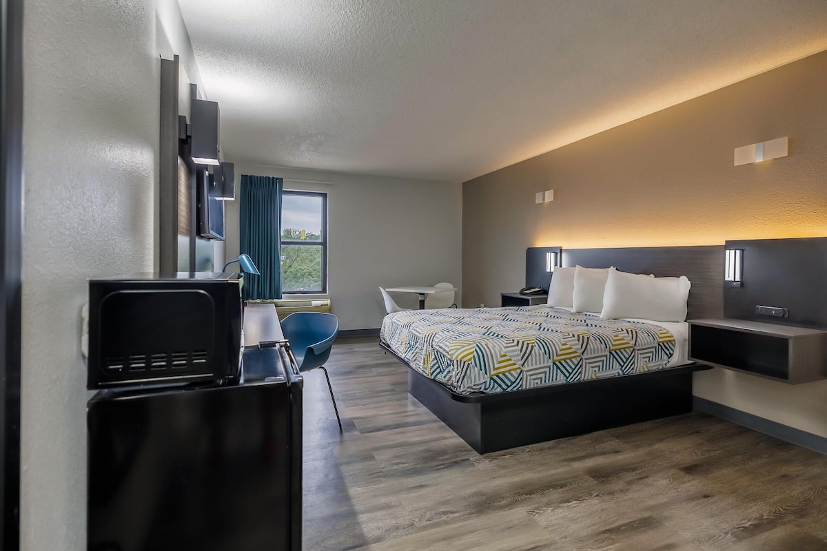 Quarto de hotel com cama, escrivaninha, cadeira e televisão.