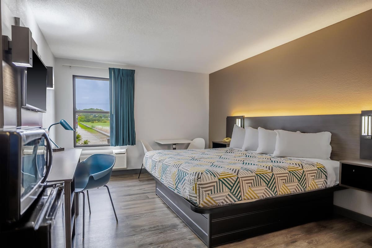 Quarto de hotel moderno com cama, escrivaninha e cadeira, televisão e uma janela grande com vista.