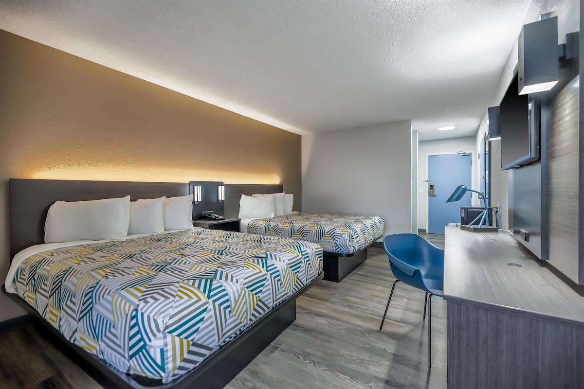 Quarto de hotel com duas camas, uma escrivaninha, uma cadeira e uma televisão.