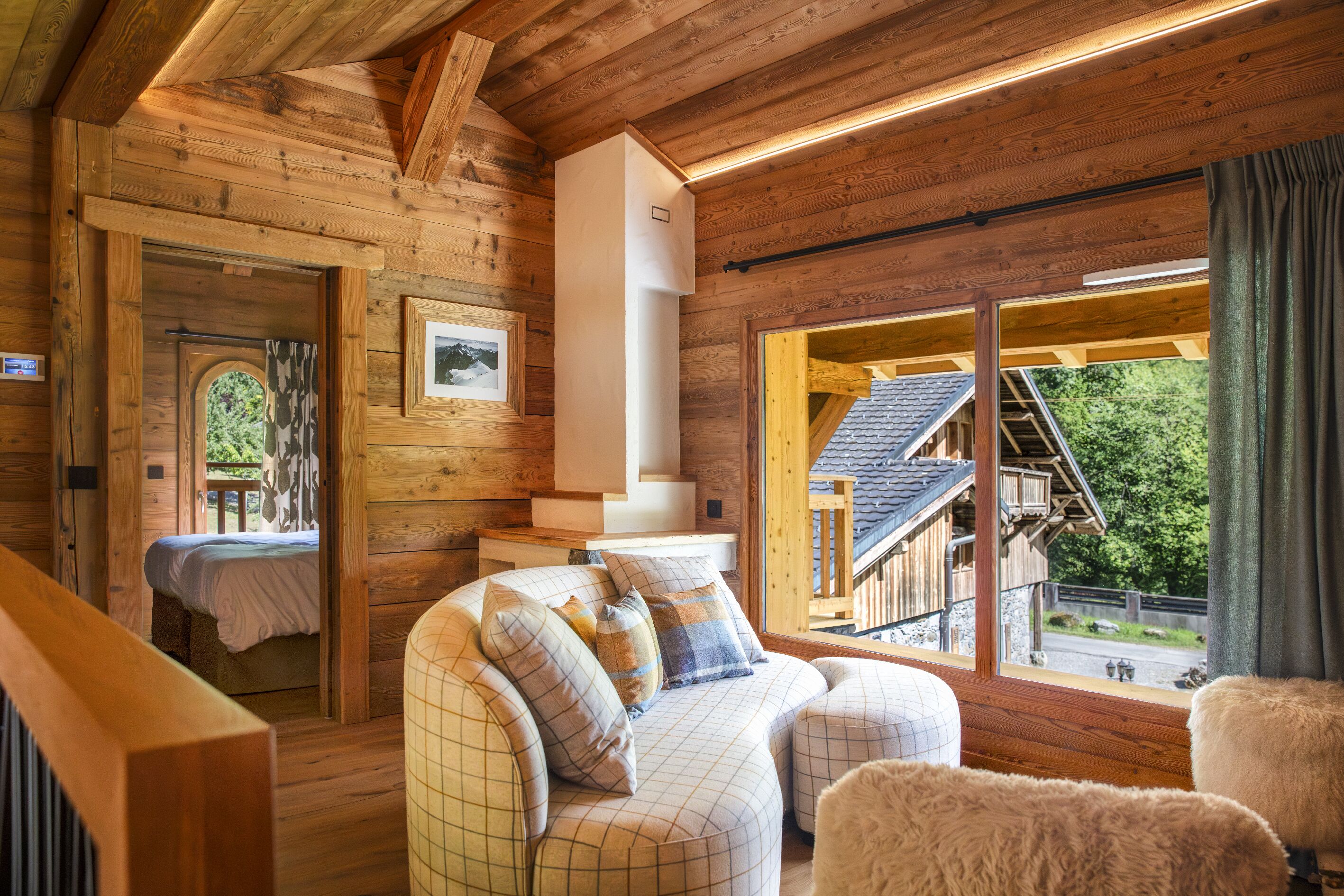 Interior de uma cabana de madeira com sofá, lareira e vista para uma montanha.