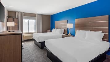 Quarto de hotel com duas camas, uma escrivaninha, uma luminária e uma janela com cortinas.