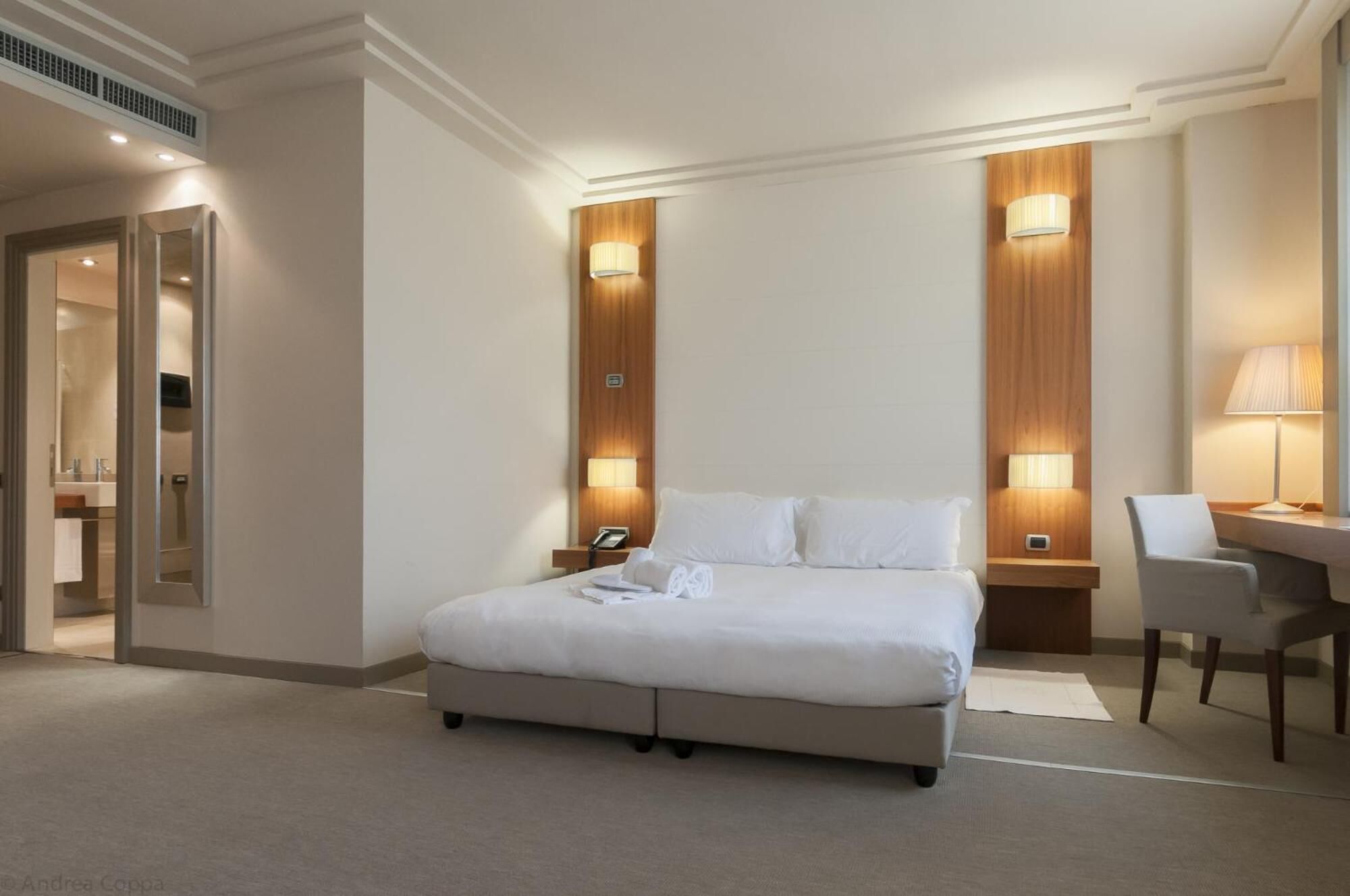 Quarto de hotel com uma cama grande, mesas de cabeceira, uma escrivaninha e uma cadeira.