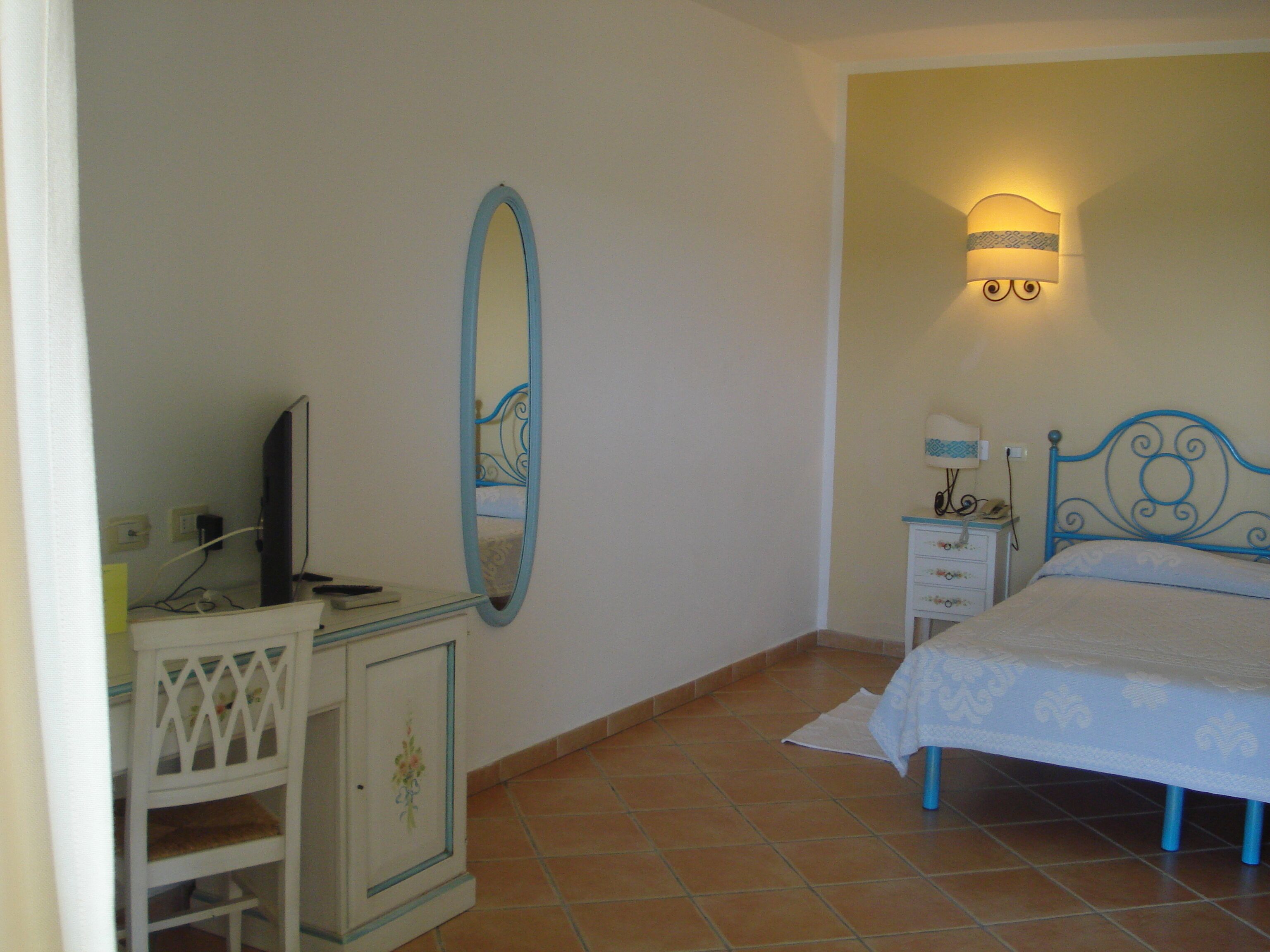 Quarto com cama, penteadeira, espelho e luminária na parede.