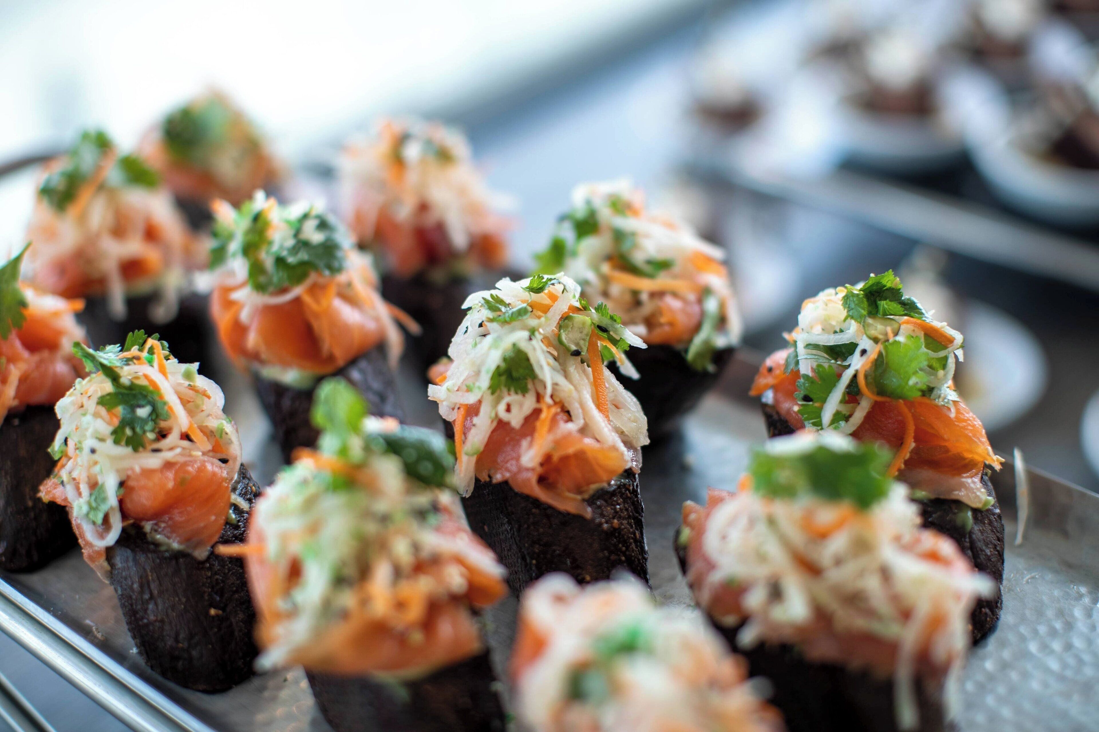 Uma travessa de aperitivos com salmão defumado e vegetais ralados sobre pão escuro.