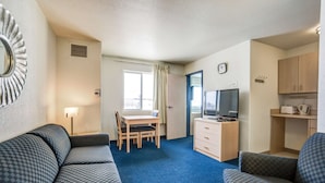 Quarto de hotel compacto com sofá, televisão, escrivaninha e cozinha compacta.