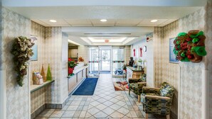 Um hall de hotel com piso ladrilhado, balcão de recepção, uma cadeira e uma decoração natalina.