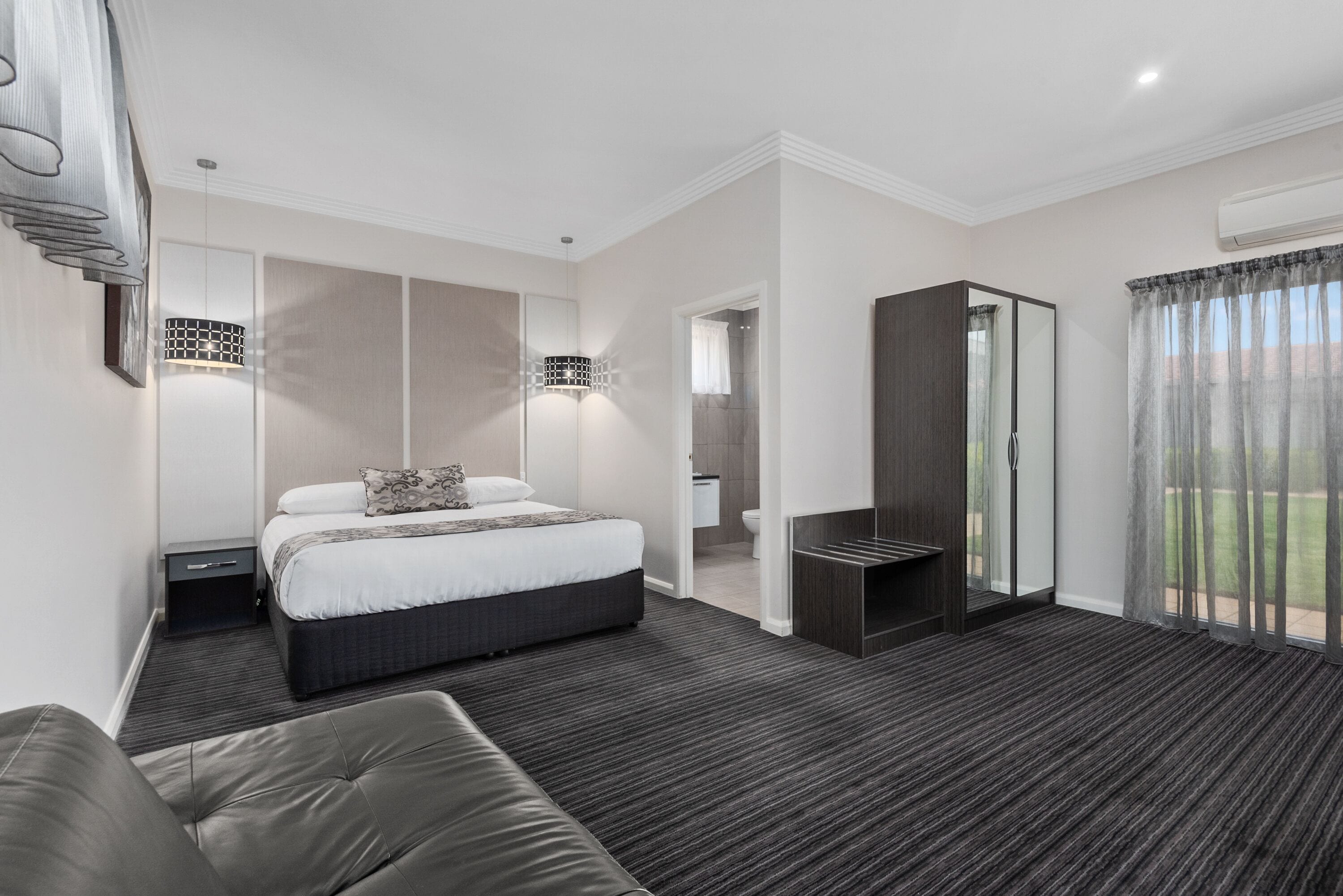 Quarto de hotel moderno com uma cama grande, um sofá, um closet espaçoso e vista para o exterior.