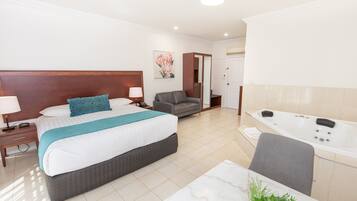 Quarto de hotel com uma cama grande, um sofá, uma escrivaninha com cadeira, banheiro com banheira e um quadro na parede.