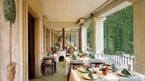Restaurante com mesas preparadas para refeições, varanda com guarda-corpo e vista para o verde lá fora.