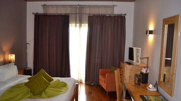 Quarto de hotel com uma cama, uma escrivaninha com computador, uma cadeira, televisão e um espelho grande.