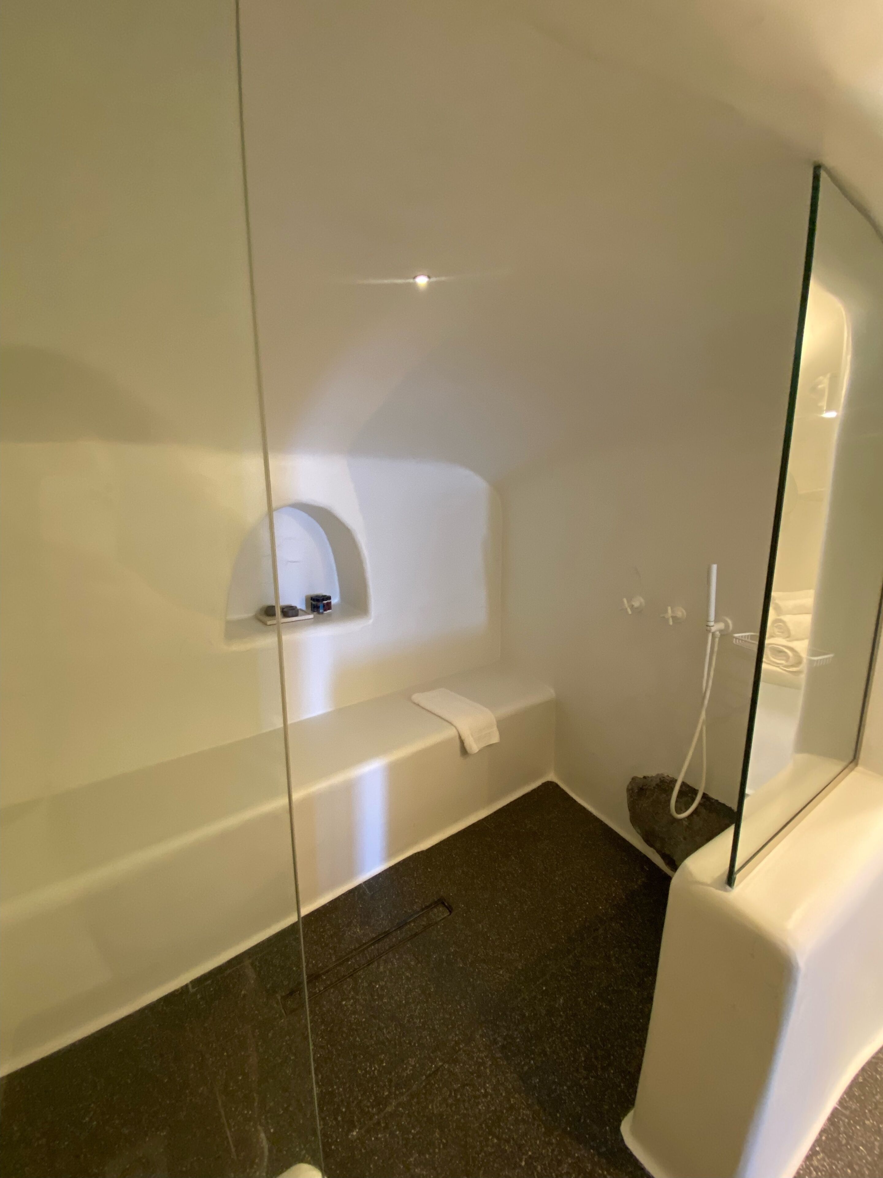 Uma casa de banho moderna com cabine de chuveiro em vidro, uma banheira branca e um pequeno armário com produtos de higiene pessoal.