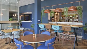 Uma área de bar moderna com cadeiras azuis e castanhas, um balcão de madeira e luminárias pendentes de cobre.
