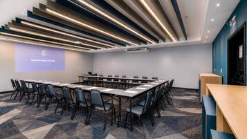 Sala de conferências com uma mesa comprida, cadeiras, tela de projetor e design moderno no teto.