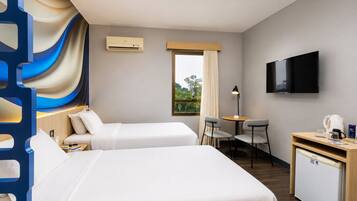 Quarto de hotel com duas camas, uma mesa com cadeira, televisão e janela com cortinas.