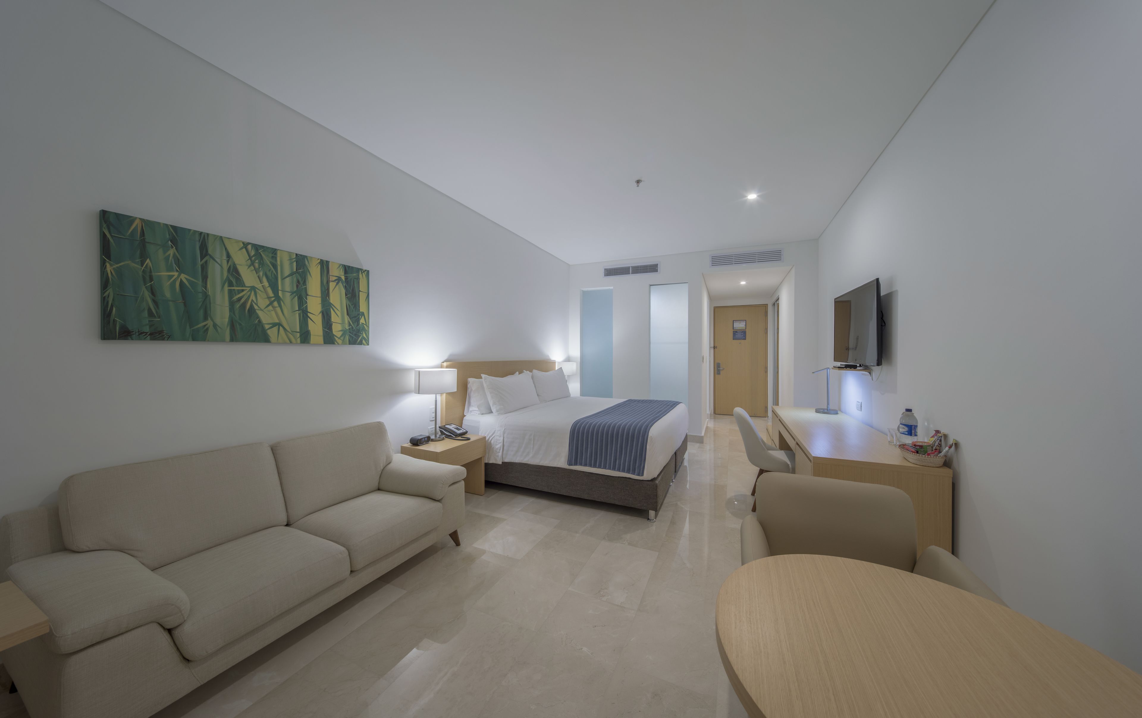 Quarto de hotel moderno com cama, sofá, escrivaninha e televisão.