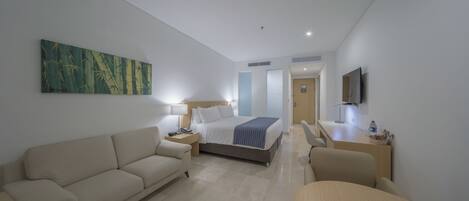 Quarto de hotel moderno com cama, sofá, escrivaninha e televisão.