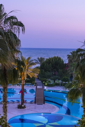 Área de piscina do resort com um caminho que leva à praia, cercada por palmeiras e espreguiçadeiras.