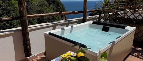 Banheira de hidromassagem em terraço com vista para o mar e a paisagem urbana.