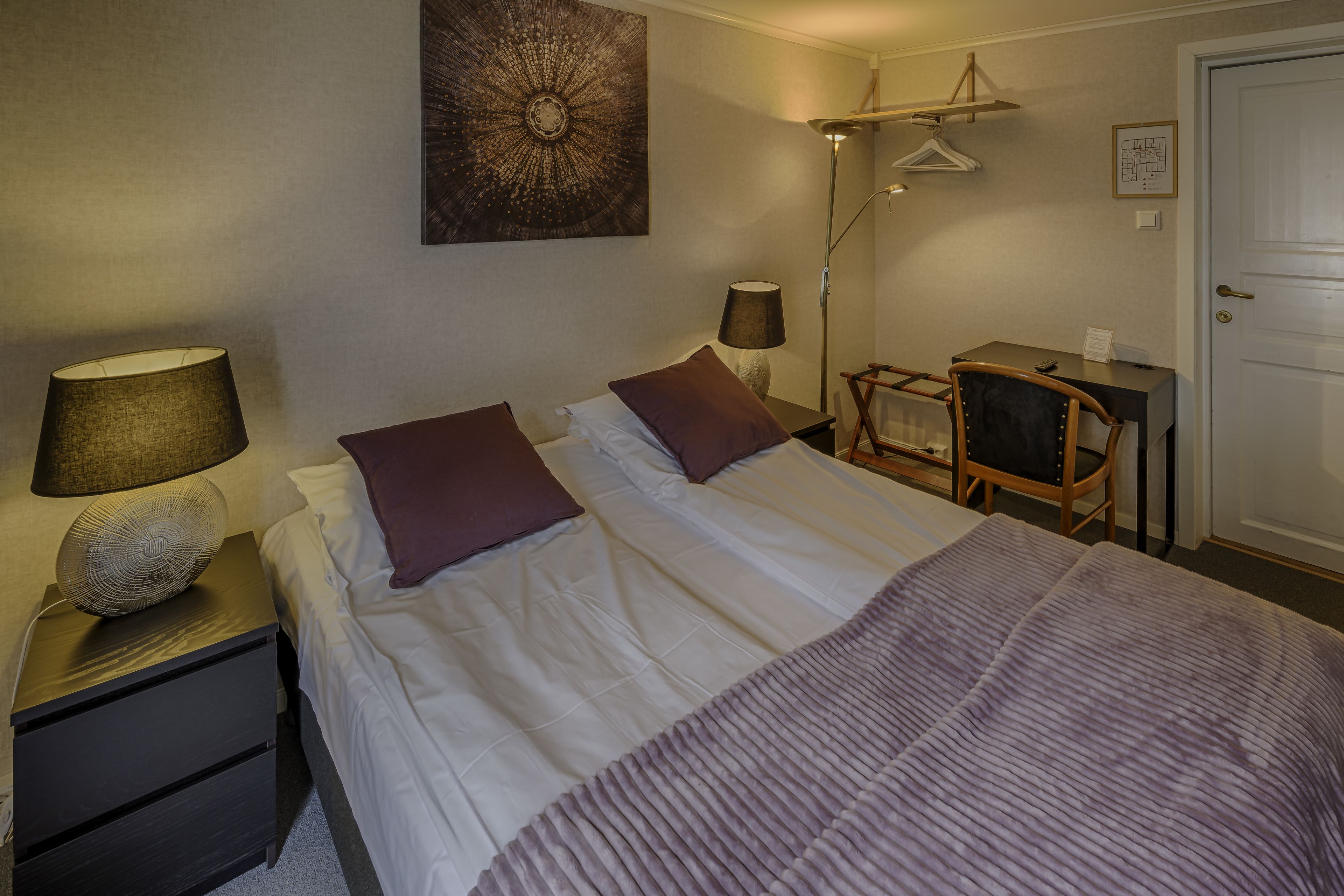 Quarto bem arrumado com cama, mesas de cabeceira, luminária, cadeira e escrivaninha.