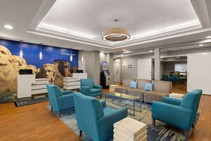 Um saguão com poltronas azul-esverdeadas, um sofá, uma mesa de recepção e um grande mural na parede.