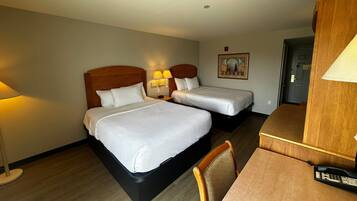 Quarto de hotel com duas camas, uma escrivaninha, uma cadeira e um abajur.