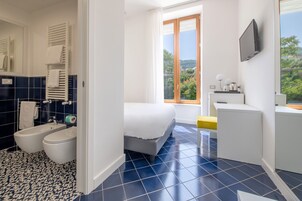 Casa de banho moderna com banheira, sanita e bidé. Tem uma janela com vista para o exterior, onde se vê vegetação.
