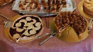 Mesa de buffet com diversos alimentos, incluindo doces, carnes e um bolo, juntamente com um vaso de orquídeas.
