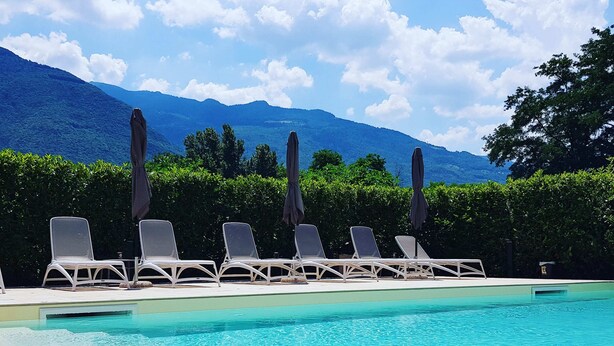 Piscina com água azul cristalina, rodeada por espreguiçadeiras e guarda-sóis, com uma paisagem montanhosa ao fundo.