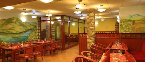 Um restaurante com mesas e cadeiras de madeira, um pilar de pedra e um mural com paisagem de montanhas.