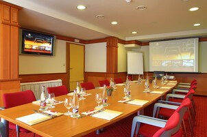 Sala de conferência com uma longa mesa montada para uma reunião, equipada com cadeiras, garrafas de água e copos.
