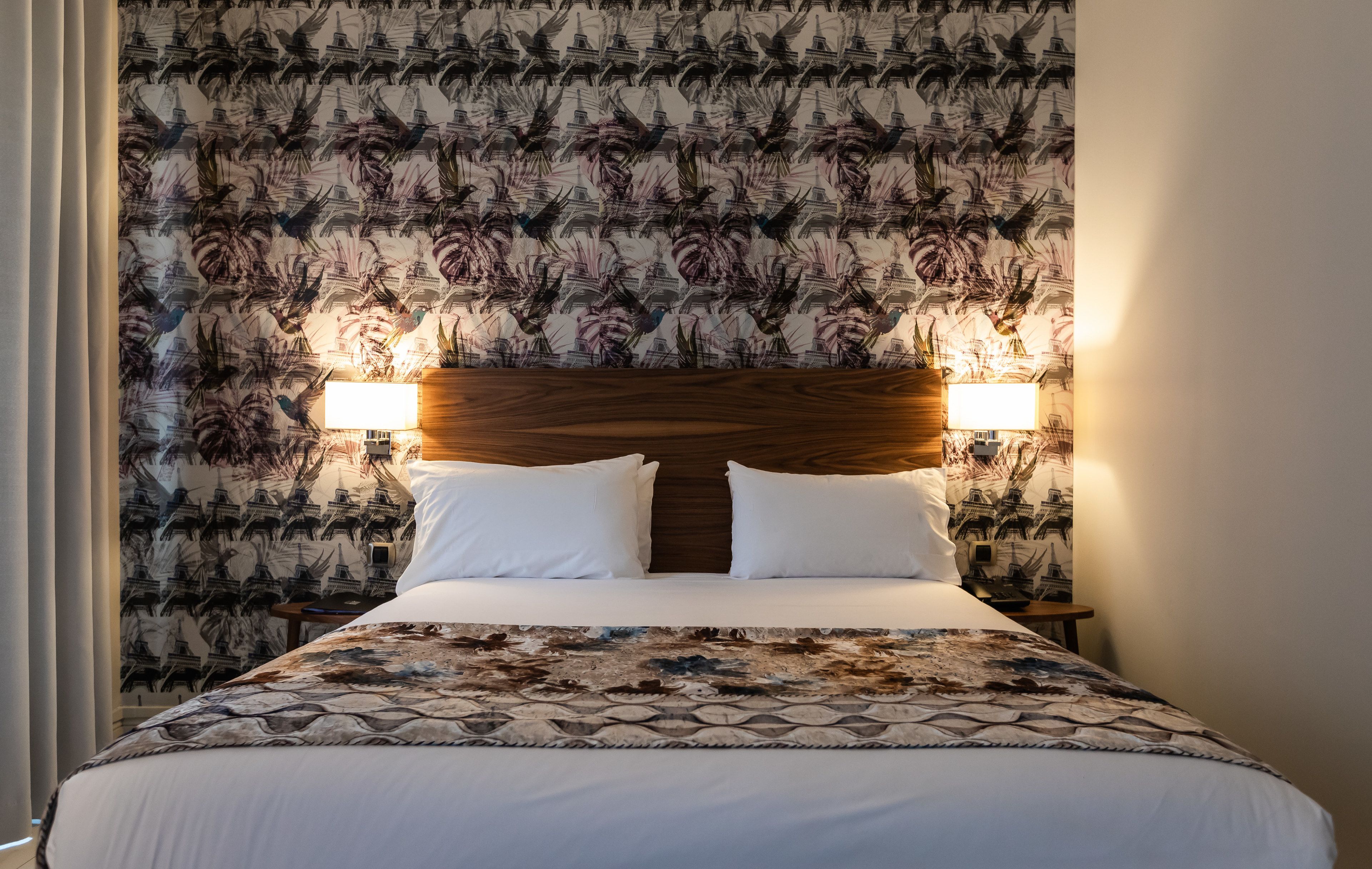 Uma cama com cabeceira estampada, duas luminárias de apoio e um manta decorativa.