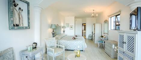 Um quarto espaçoso com uma cama grande, uma área de estar com uma mesa e cadeiras, e um closet amplo.