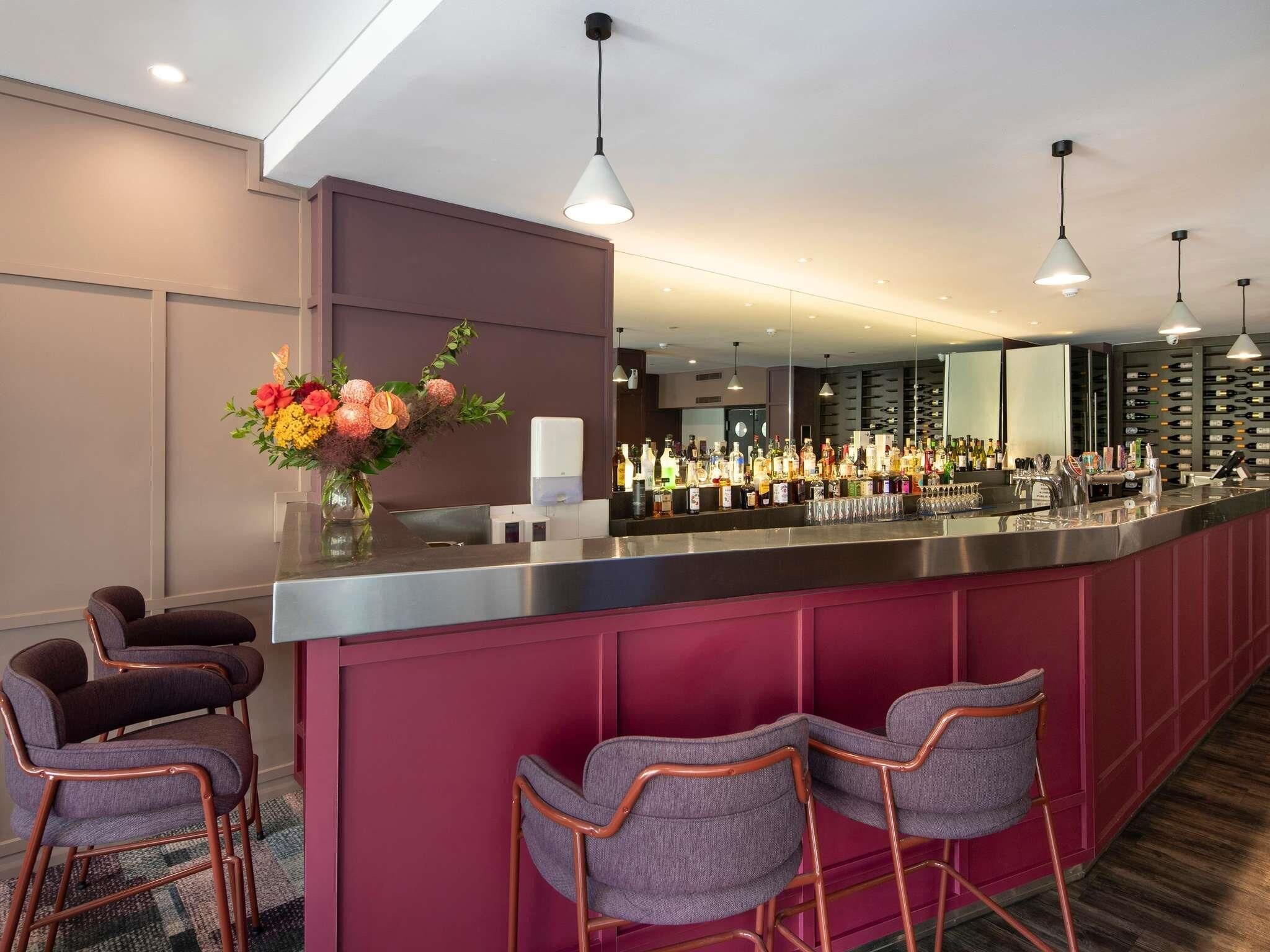 Uma área de bar com balcão, banquetas e diversos tipos de garrafas.