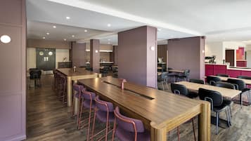 Uma sala de conferências moderna com mesas longas e cadeiras roxas, uma área de cozinha e um bar.