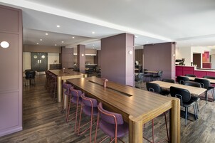 Uma sala de conferências moderna com mesas longas e cadeiras roxas, uma área de cozinha e um bar.
