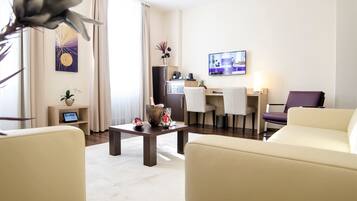 Quarto de hotel moderno com sala de estar, mesa de jantar, cozinha e televisão presa na parede.