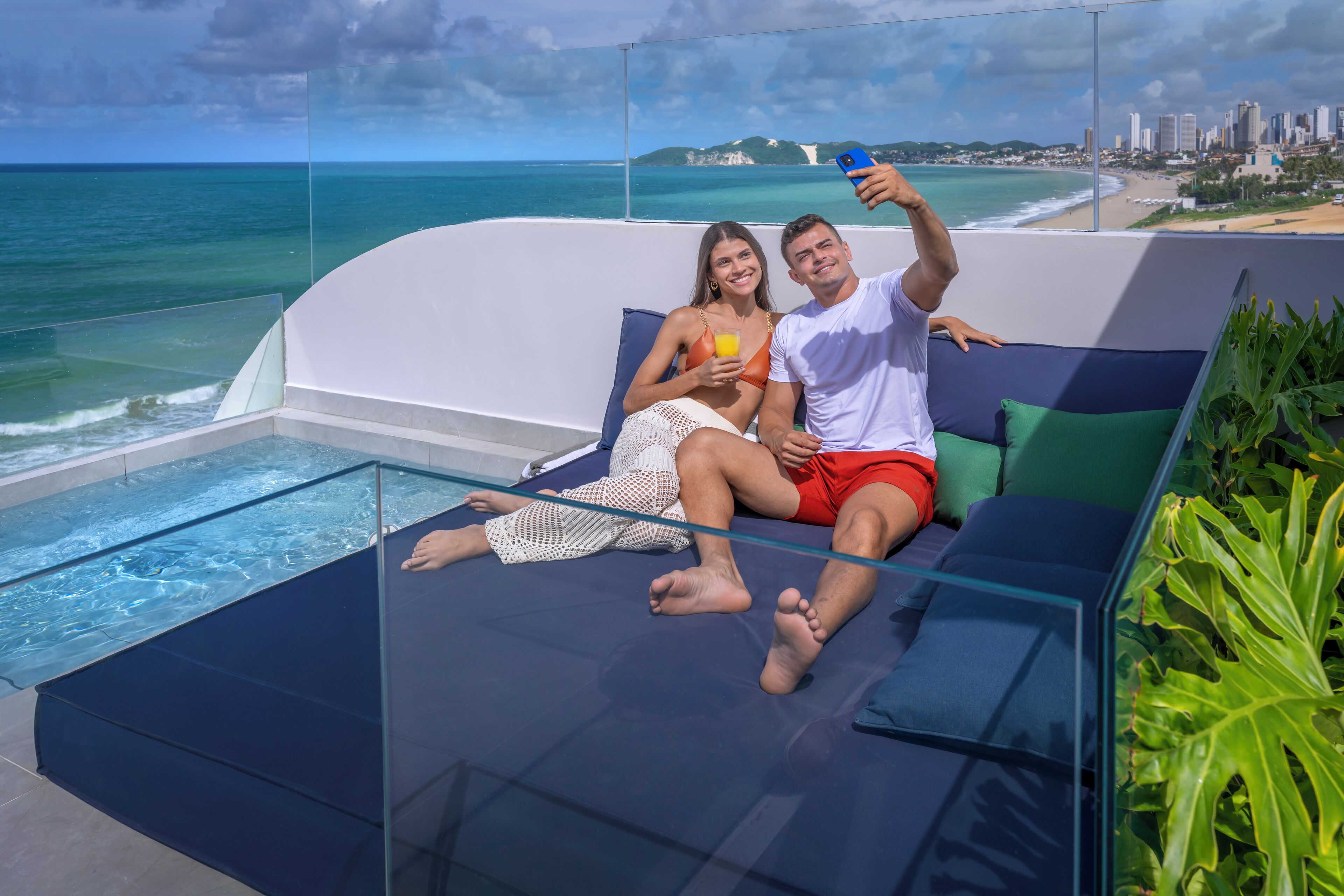 Um casal relaxando numa varanda envidraçada com vista para a cidade e para a praia.