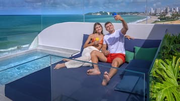 Um casal relaxando numa varanda envidraçada com vista para a cidade e para a praia.