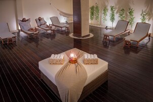 Um quarto de spa com piso de madeira, cadeiras de descanso, cama com toalhas e um pilar central.