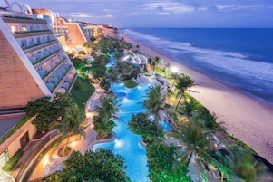Resort com piscina, palmeiras e vista para a praia.