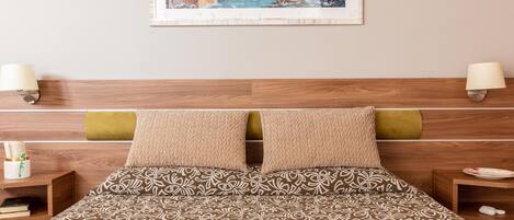 Cama bem arrumada com roupa de cama estampada, cabeceira de madeira e duas mesas de cabeceira com abajures.