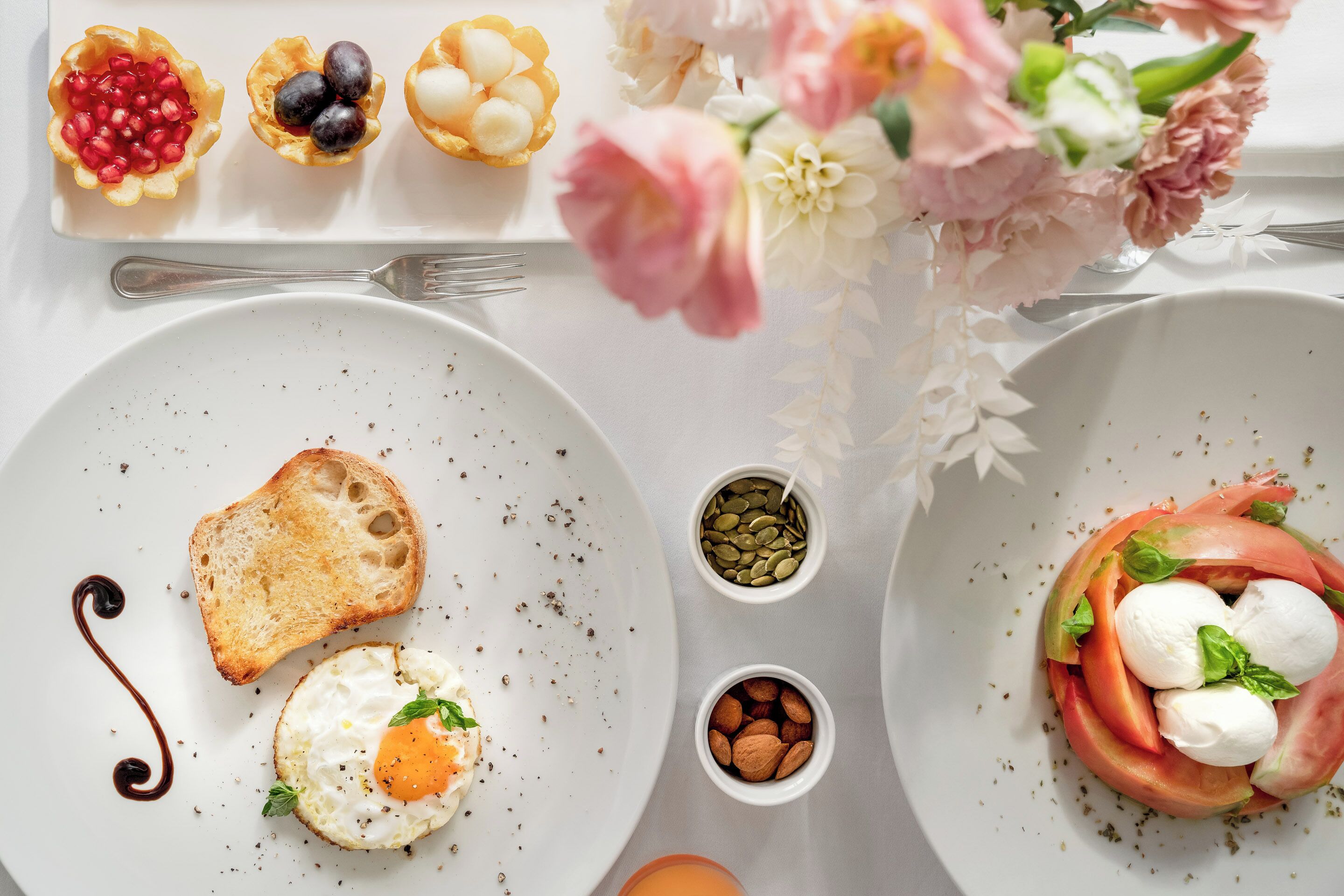 Uma mesa de café da manhã com torradas, ovos e uma torta de fruta em um prato branco, acompanhada por um vaso de flores.