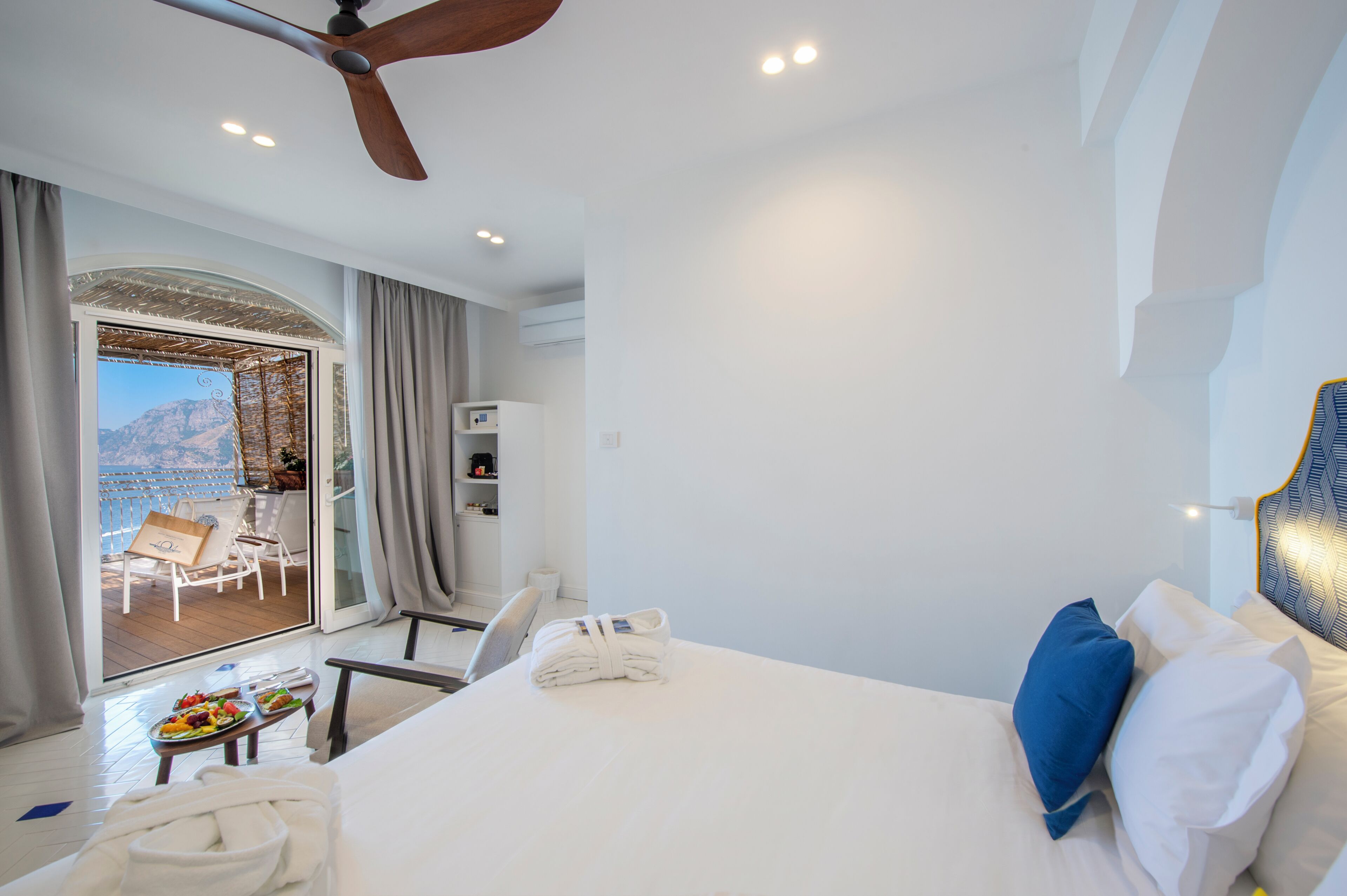 Quarto de hotel com cama, escrivaninha, cadeira, varanda e ventoinha no teto.