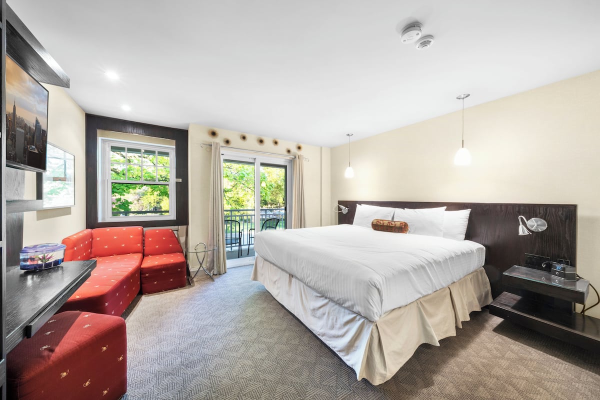 Quarto de hotel com uma cama grande, um sofá vermelho, uma escrivaninha e uma janela com vista para o verde.