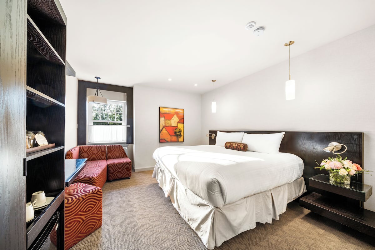 Quarto de hotel moderno com uma cama grande, um sofá, uma escrivaninha e uma estante de livros.